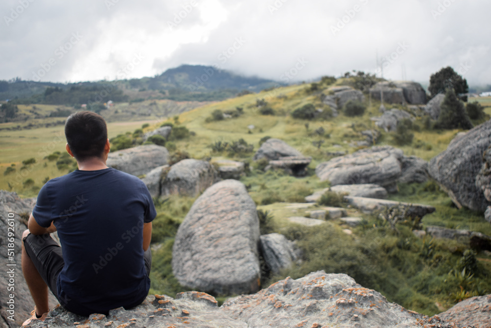 Joven sentado en una zona rocosa observando el paisaje de antiguas ...
