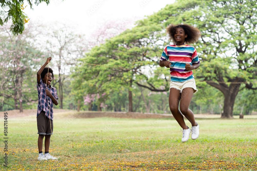 African American girl playing jumping over the rope in the park. Young ...
