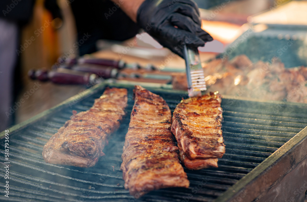 Barbecue ribs. Man in gloves flips grilled ribs on a charcoal grill ...