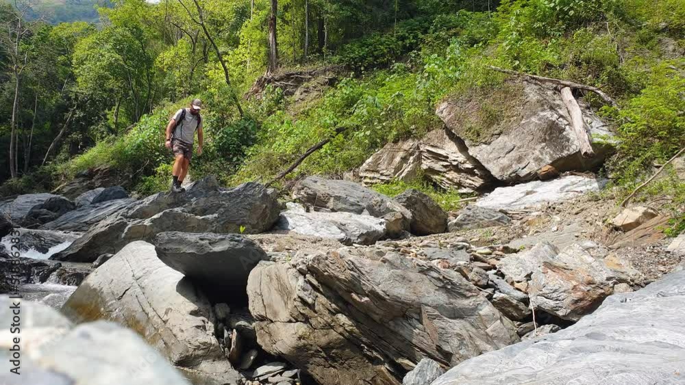 Man walking over rocks and boulders near a free flowing river in a deep ...