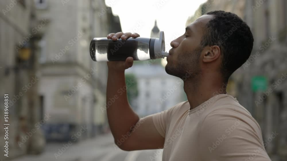 Side view african american runner drinking water from the sport bottle ...