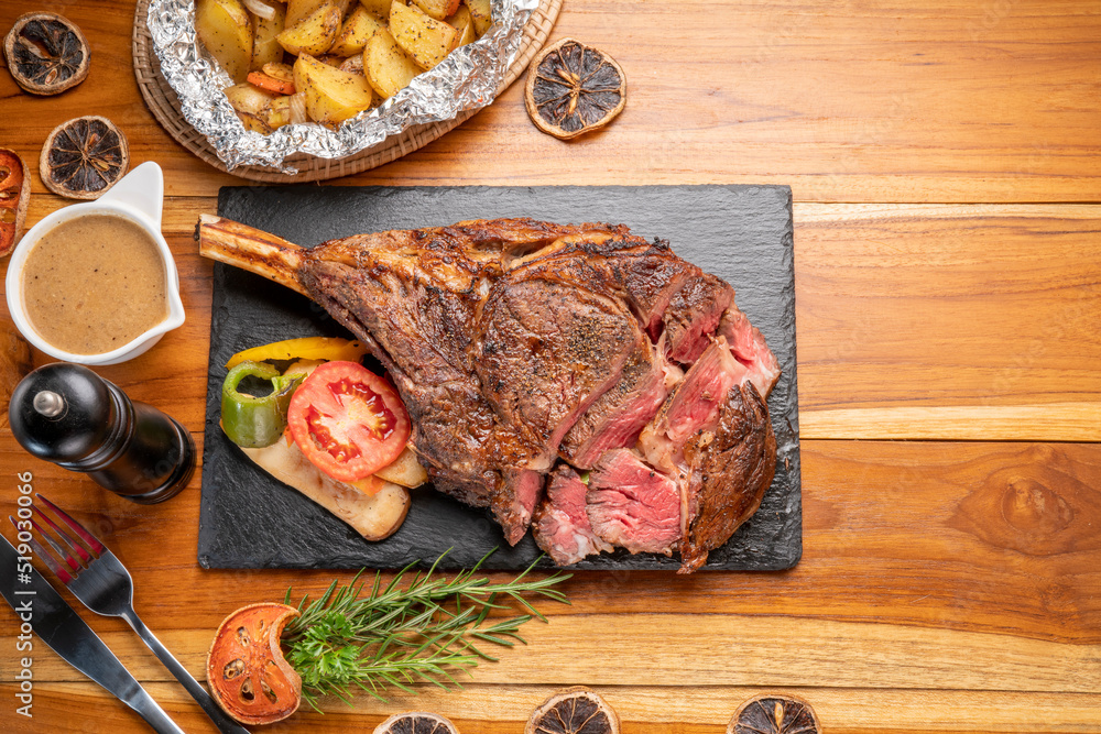 Grilled tomahawk ribeye steak in black stone plate on wooden table ...