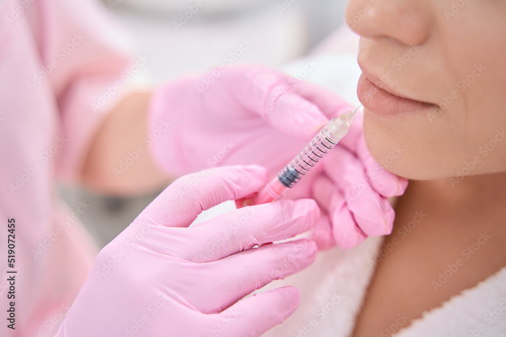 Doctor injects syringe with cosmetic product into lower lip of patient ...