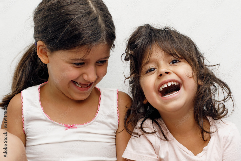 Two caucasian girls sisters have fun and laugh while sitting on the bed ...