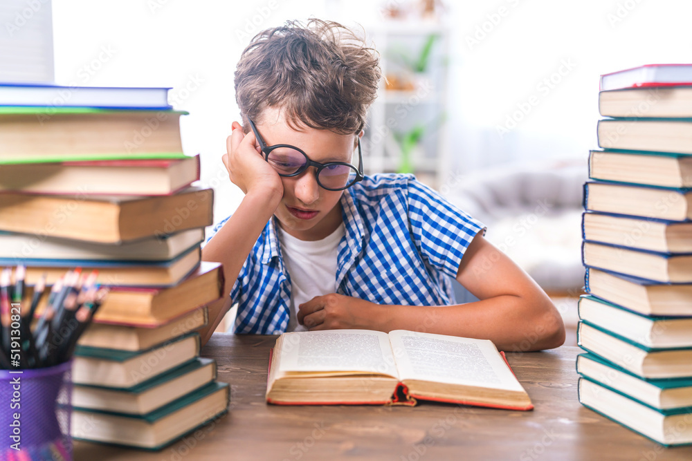 schoolboy tired of learning, wearing glasses, doing homework, sitting ...