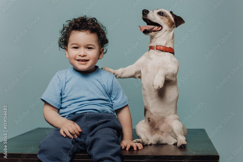 Little boy with curly hair in casual dancing on the table with a dog ...