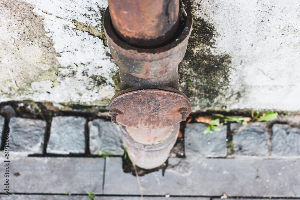 Old rain gutter with rust ending on a paved sidewalk in an urban area ...