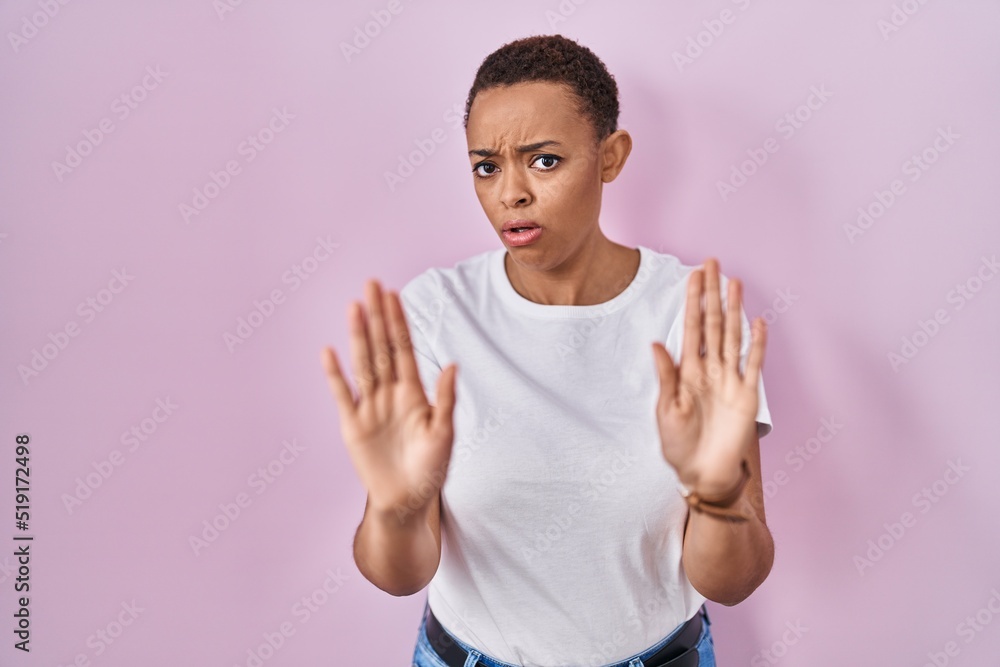 Beautiful african american woman standing over pink background moving ...
