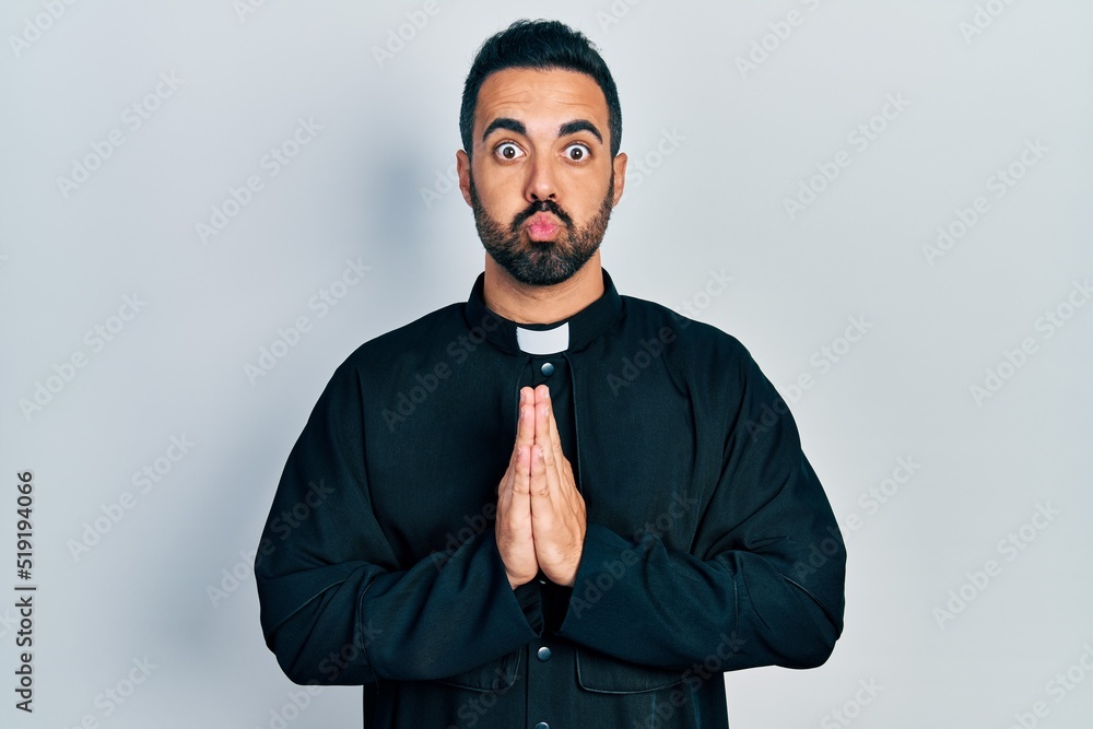 Handsome hispanic priest man with beard standing over isolated ...