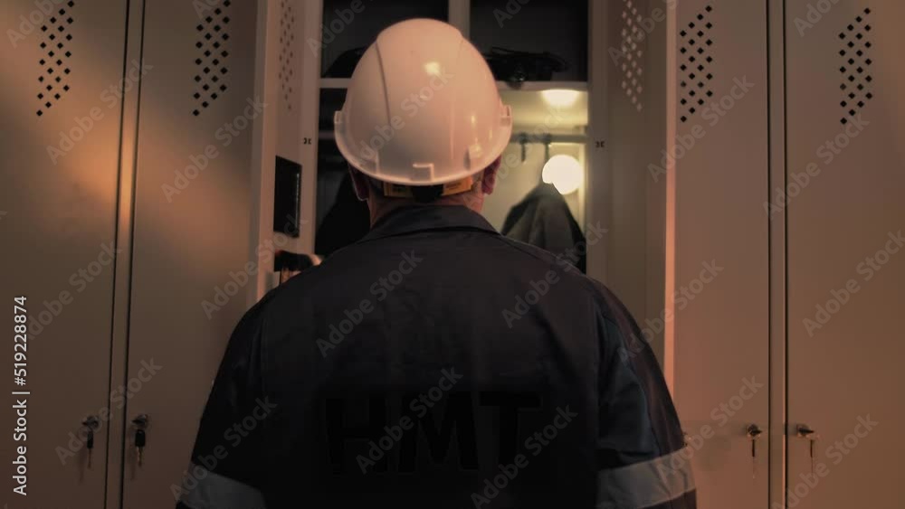 Oil refinery worker stands at his open locker in the locker room and ...