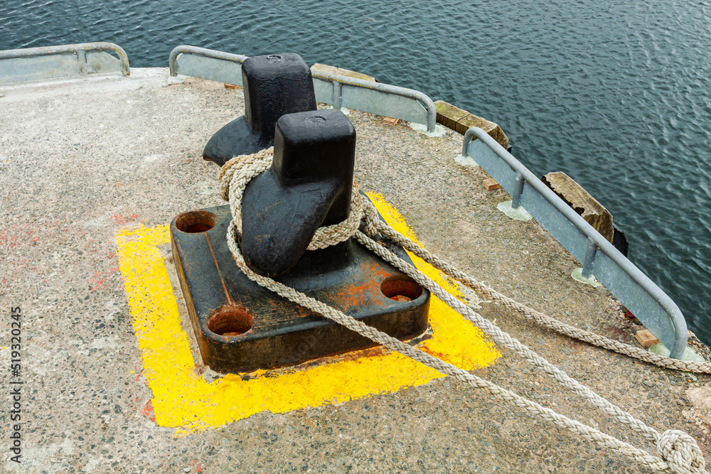 Mooring cable tied to an iron bollard on a concrete dock, boat cable ...
