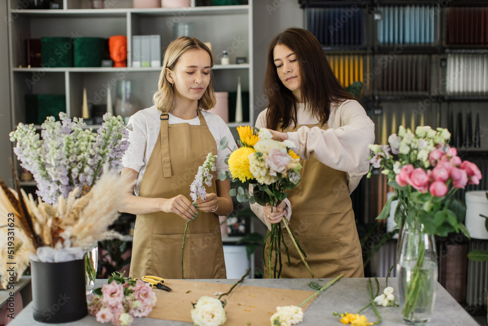 Concentrated female colleagues in aprons working together in flower ...