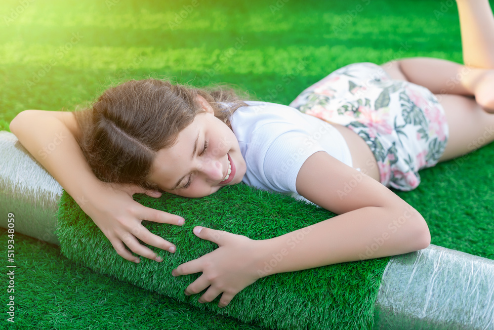 Smiling young caucasian girl lying on a new roll of artificial turf ...