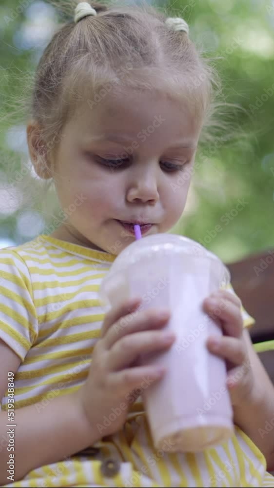 VERTICAL VIDEO: Little girl drinks a milkshake through a straw. Close ...