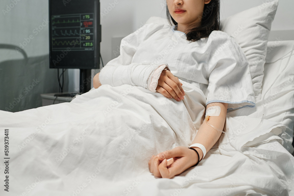 Horizontal shot of young Asian woman with arm in cast lying on hospital ...