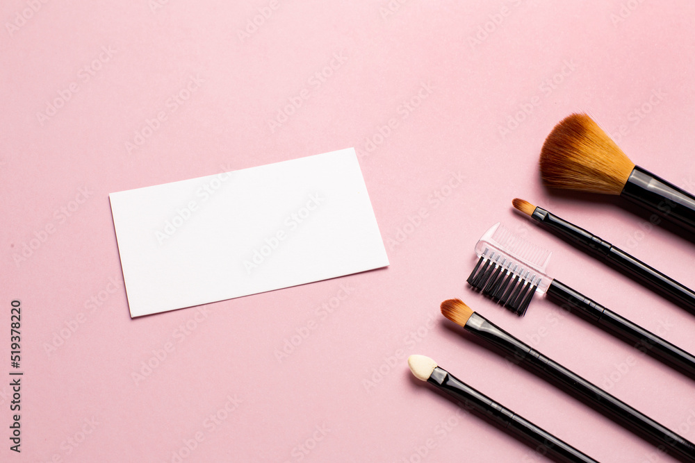 Makeup brush and white business card on pink background. A horizontal ...