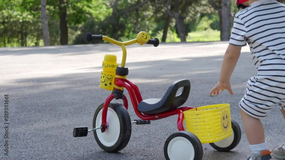 Mother teaching little child to ride tricycle for kids outdoors ...