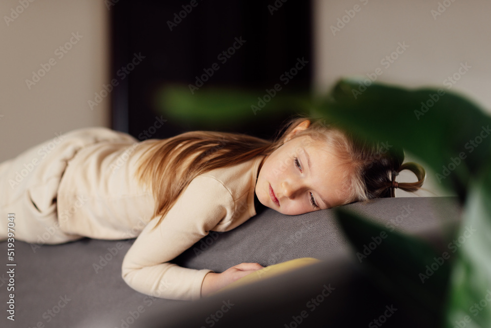 Sad little caucasian girl lying alone on couch in modern apartment and ...