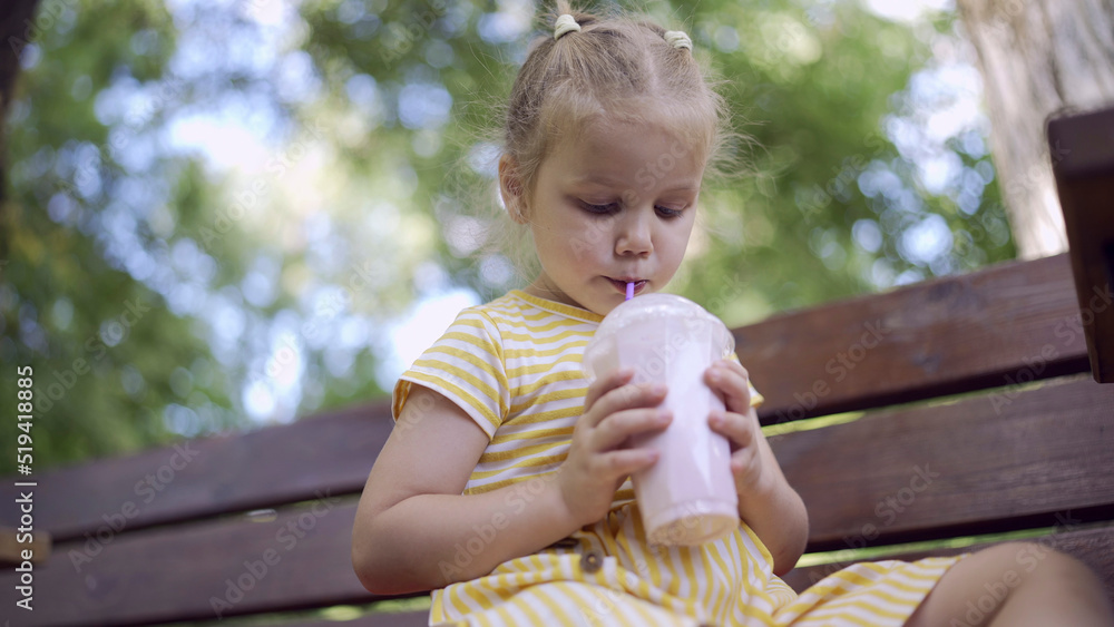 Little girl drinks a milkshake through a straw. Close-up portrait of ...