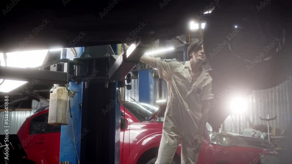 woman mechanic in a car service on a special car lift raises the car ...