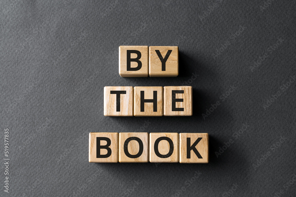 By the book - phrase from wooden blocks with letters, according to the ...