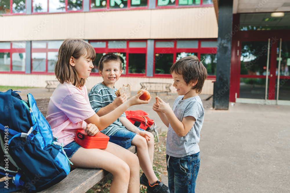 Children sit on a bench in the school yard and eat apples and ...