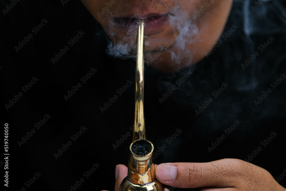 Asian man smokes marijuana from a pipe at home. Studio shoot with model ...