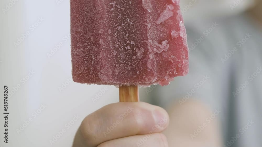 A hand brings a blueberry popsicle closer to the camera, detail and ...