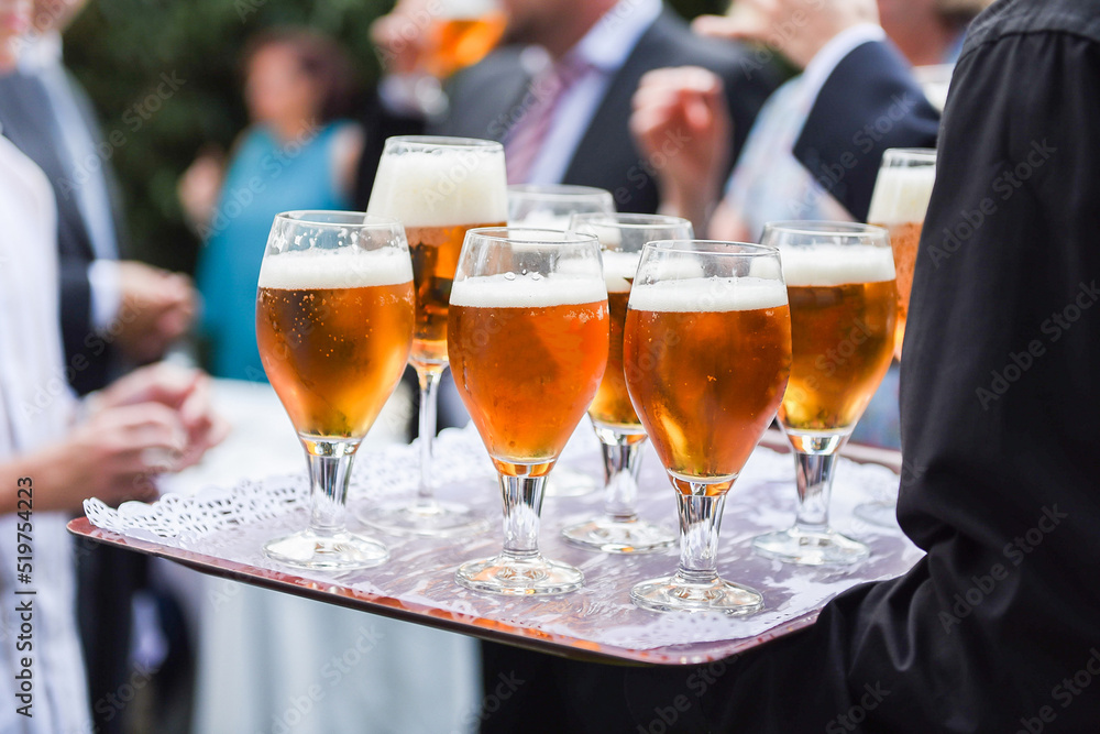 Waiter serving several beers in glasses on a tray to guests at an event ...