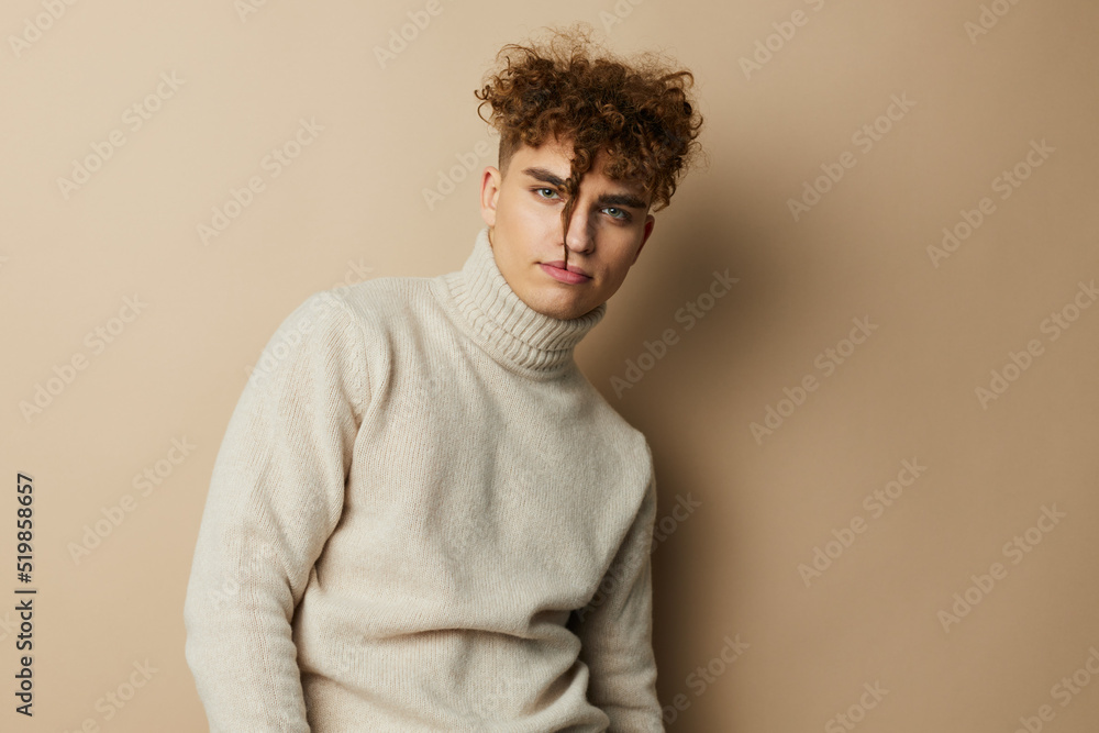 Man With Curly Hair Standing On Beige Background In Light Turtleneck Looking Pleasantly Into