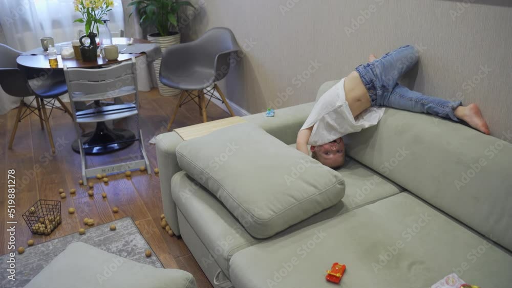 Cute child messing around at home in kitchen, lying on couch, throwing ...