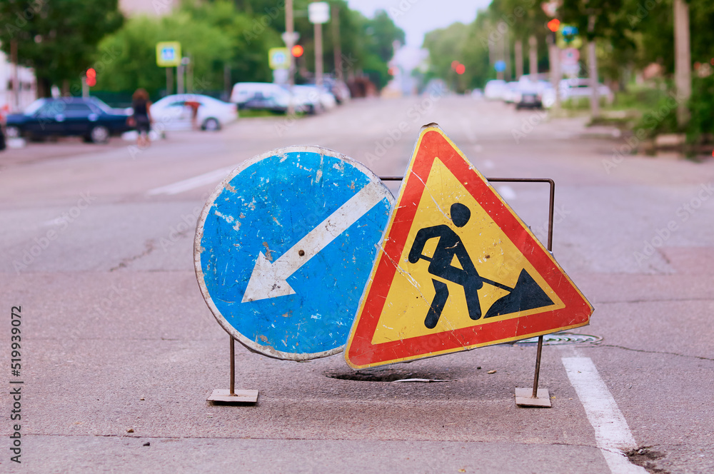 A metal frame with worn, scratched road works and bypass road signs ...