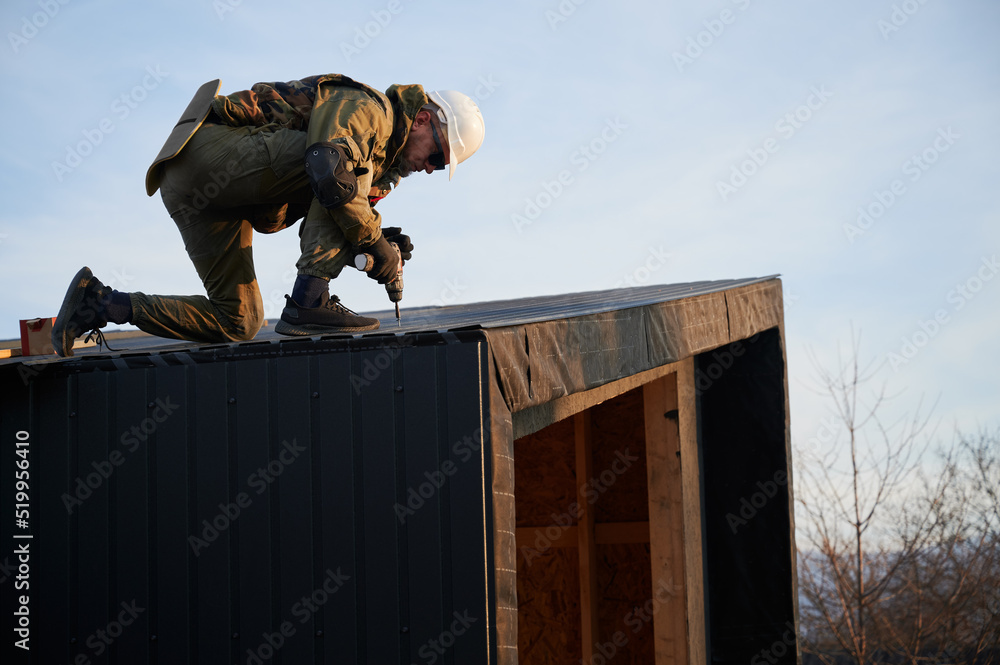 Male builder installing black corrugated iron sheet used as facade of ...