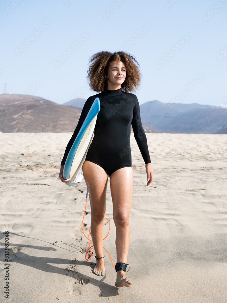 Pretty young surfer female with afro hair walking to the waves with her ...