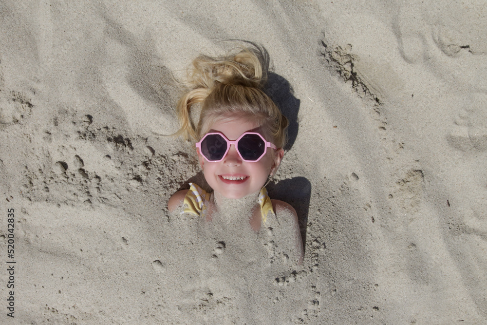 Cute happy little girl buried in the sand on the beach. Stock Photo ...