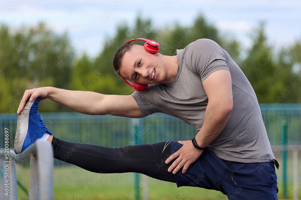 Muscular athlete stretches hamstring stadium field while listening ...