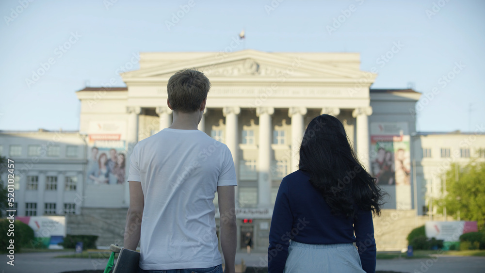 Rear view portrait of two students carrying walking and look at the ...