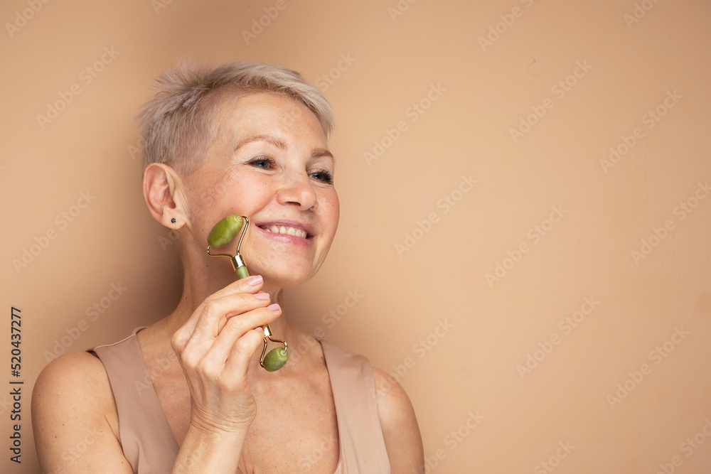 Gorgeous woman of 60s massaging face skin using natural facial stone ...