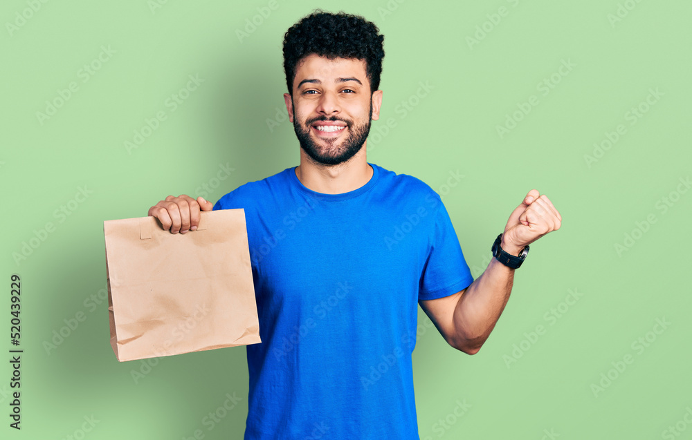 Young arab man with beard holding take away paper bag screaming proud ...