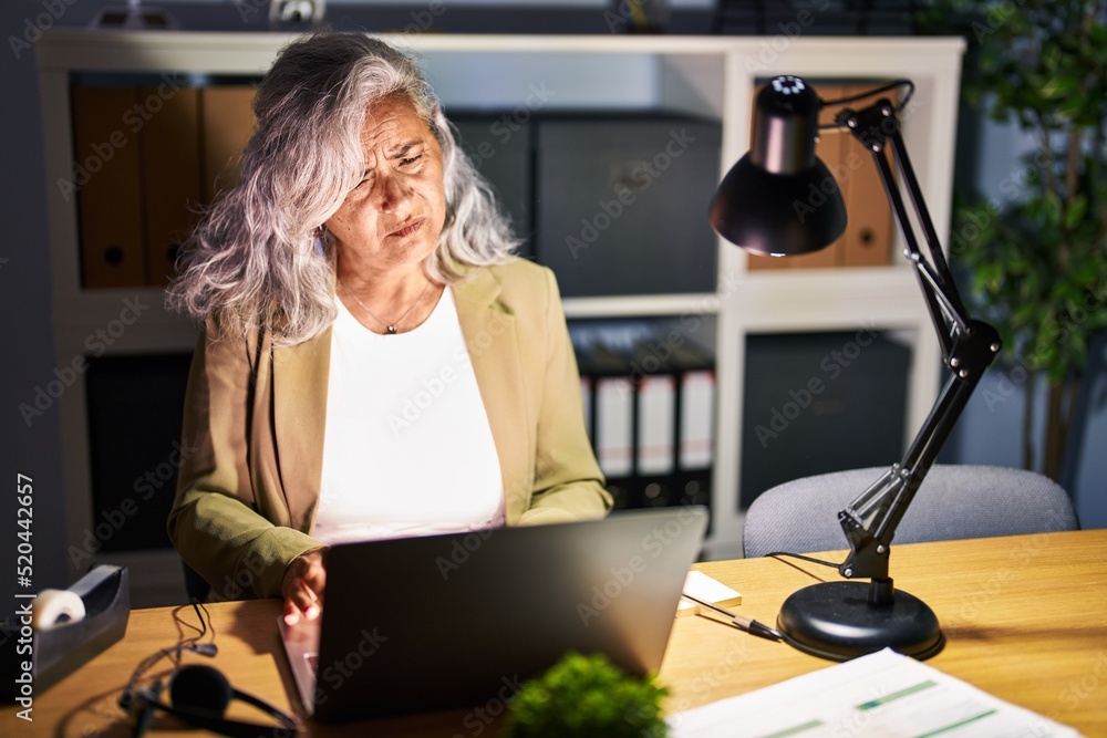 Middle age woman with grey hair working using computer laptop late at ...