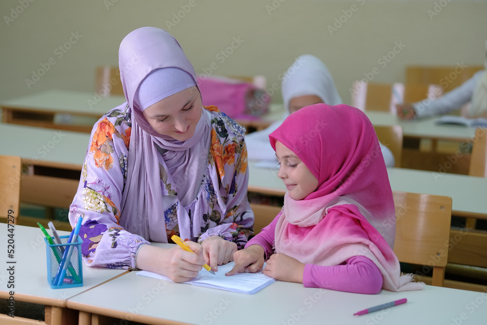 Female hijab Muslim teacher helps school child to finish the lesson in ...