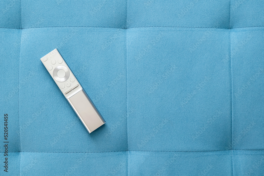 One single simple sliver smart TV remote control laying on a blue sofa ...