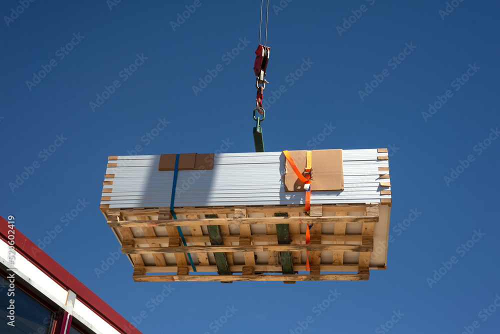 A crane lifts a stack of solar panels to the roof for installation ...