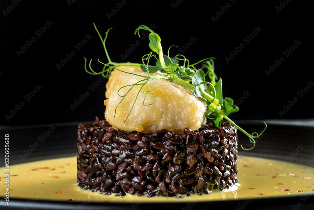 Risotto with slice roasted white fish, cod on black background. Grilled ...
