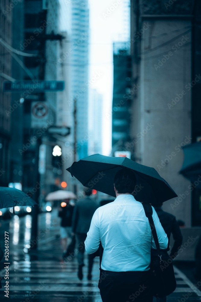 Vertical back view of a male walking in the street with an umbrella on ...