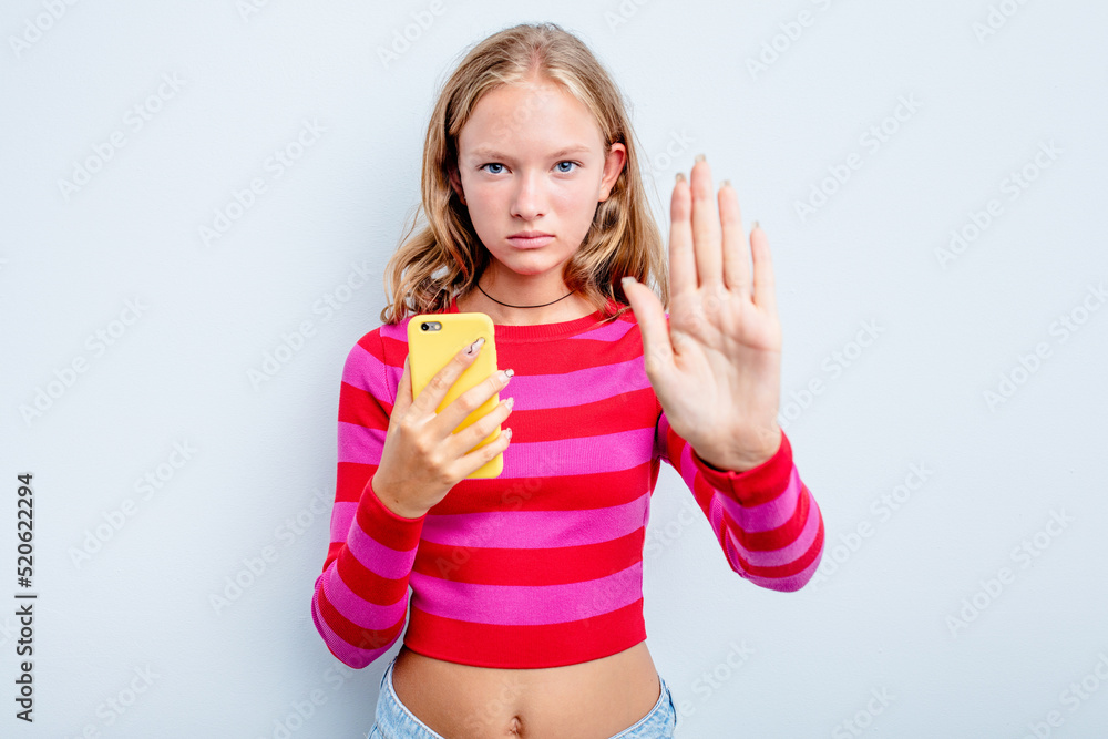 Caucasian teen girl holding mobile phone isolated on blue background ...