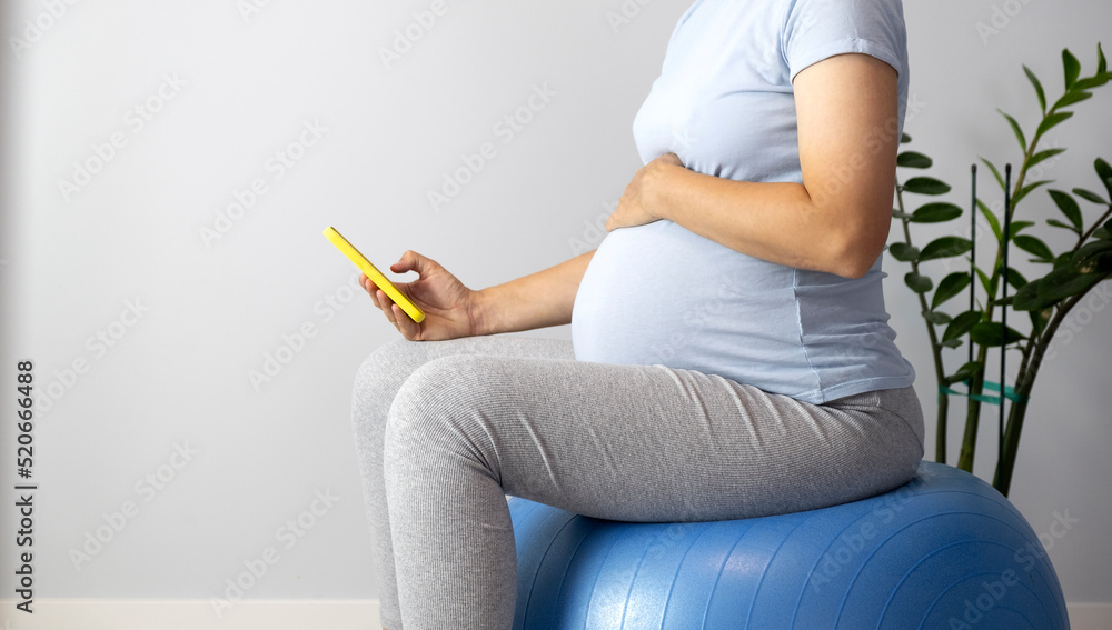 Pregnant woman feel contractions sitting on fitball and use mobile time ...