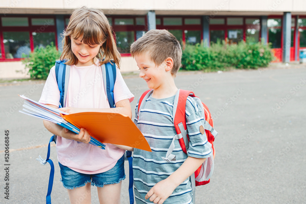 Schoolchildren, a girl and a boy, share notebooks in the school yard ...