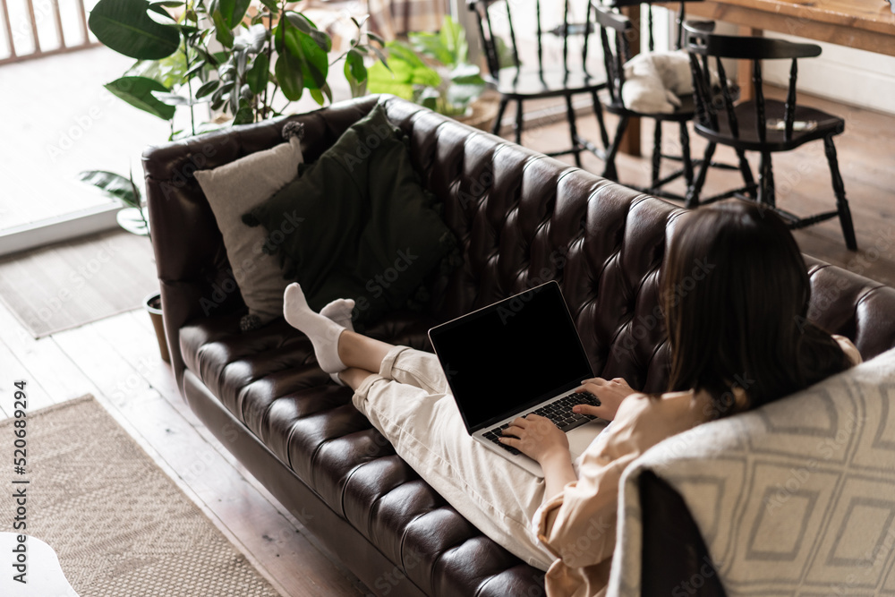 Rear view of young woman relaxing at home with laptop. Girl sits on ...