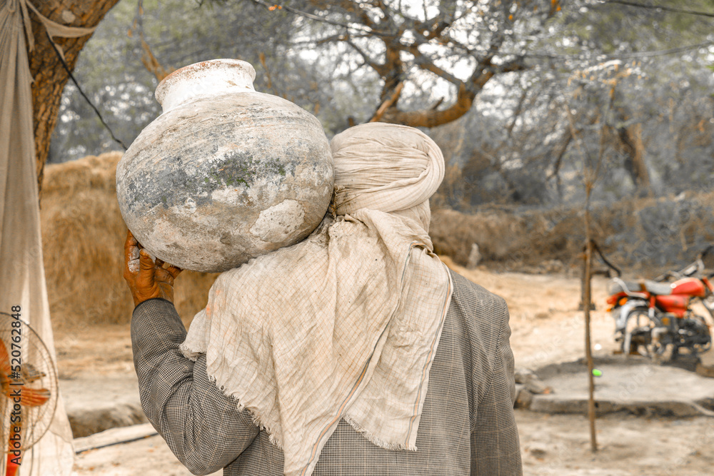 an older man carrying a water pot on his shoulder in a cause of water ...